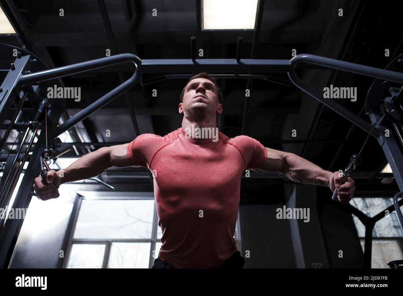 Low angle shot of a muscular bodybuilder working out in cable crossover ...