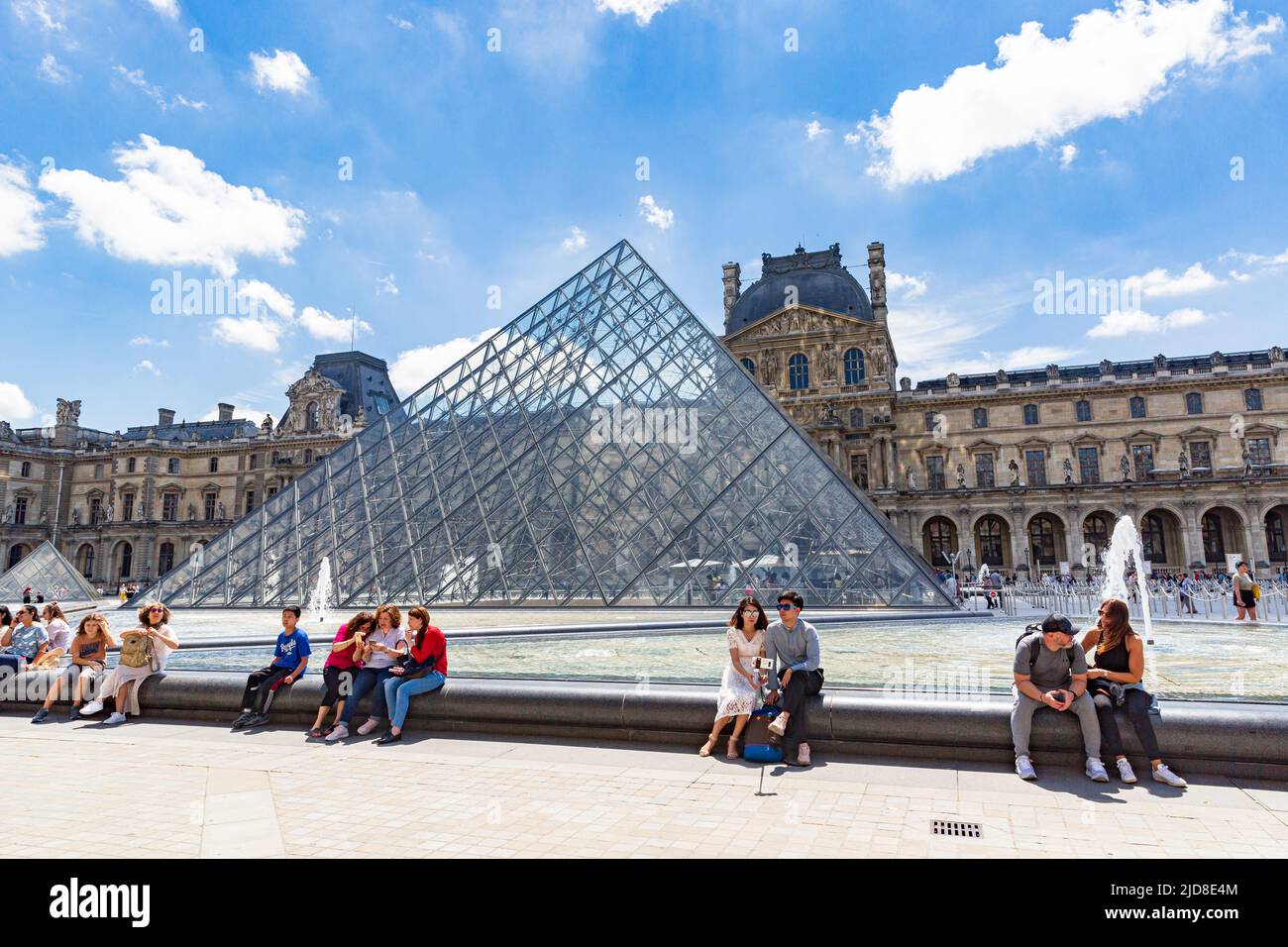 tired tourists rest sitting by the fountain next to the Louvre museum ...