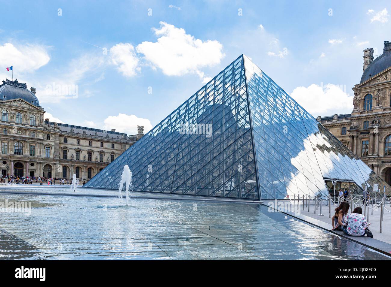 tired tourists rest sitting by the fountain next to the Louvre museum ...