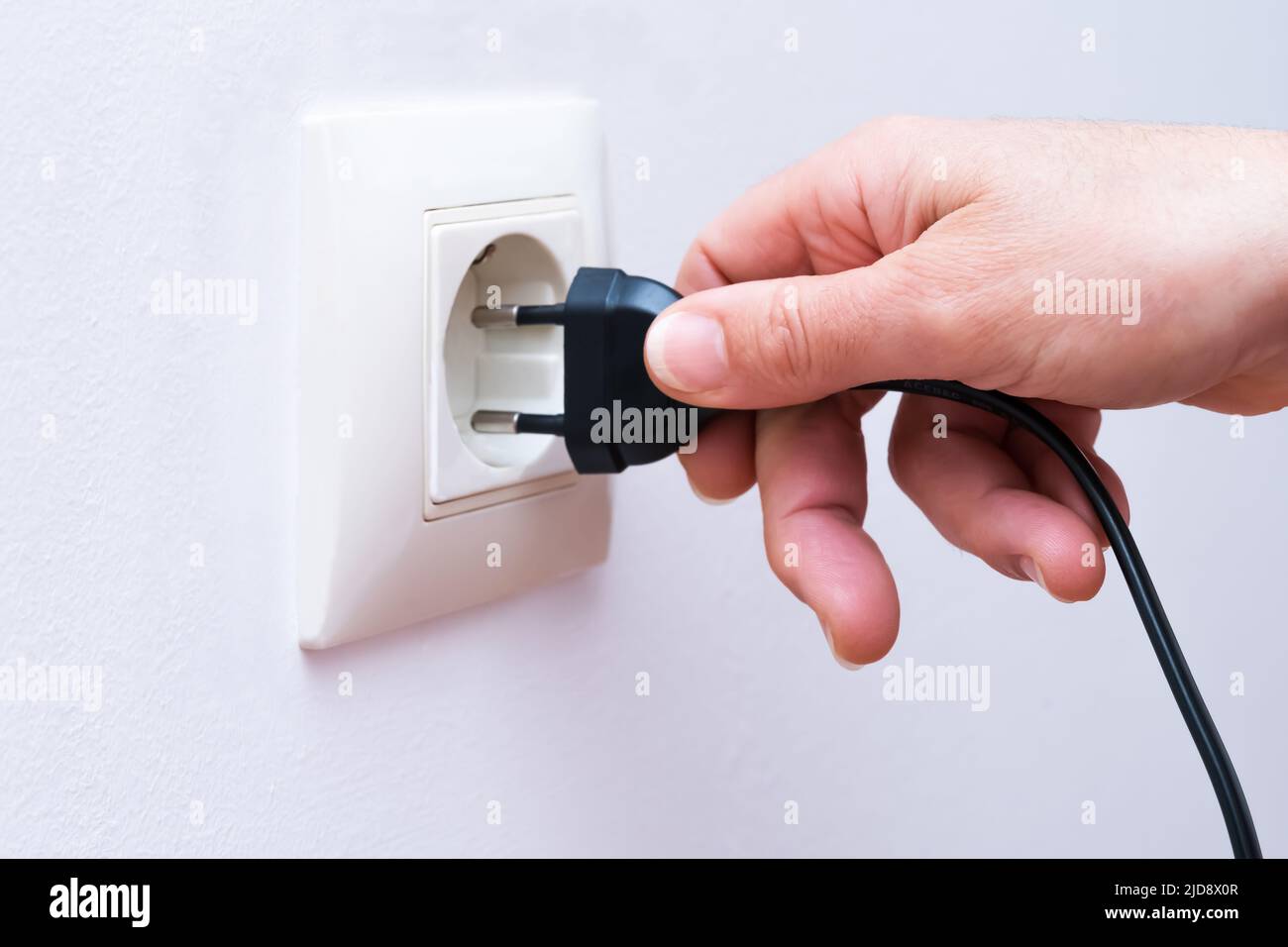 Plugging a black electrical plug into a wall socket with a woman's hand ...
