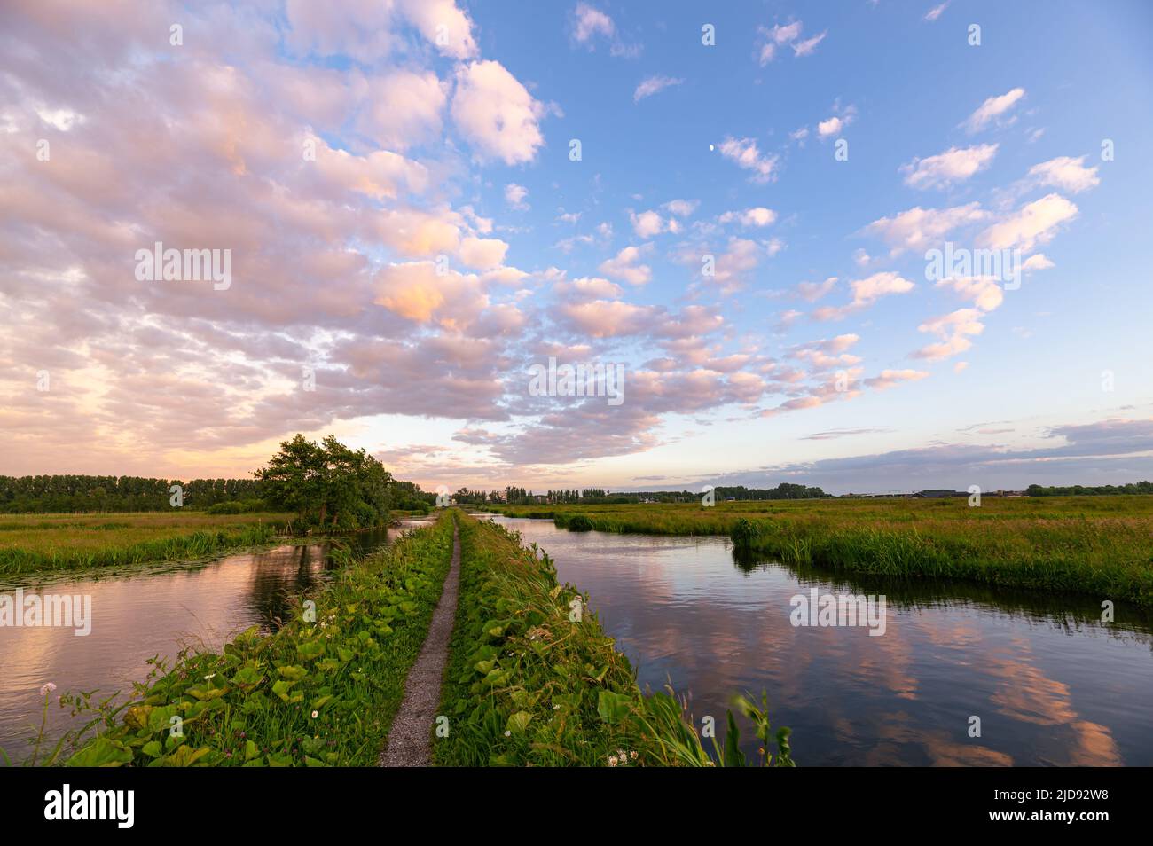 Scenic view of a small path on a dike below a colorful sky in polder ...