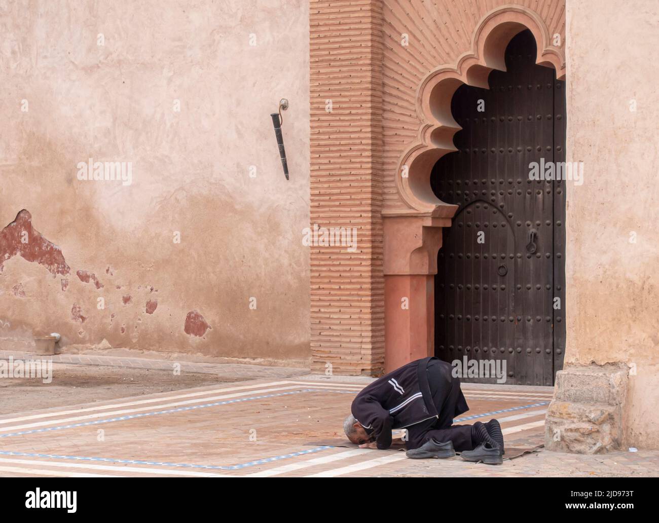 Muslim Moroccan man praying on his knees in front of the ancient ...
