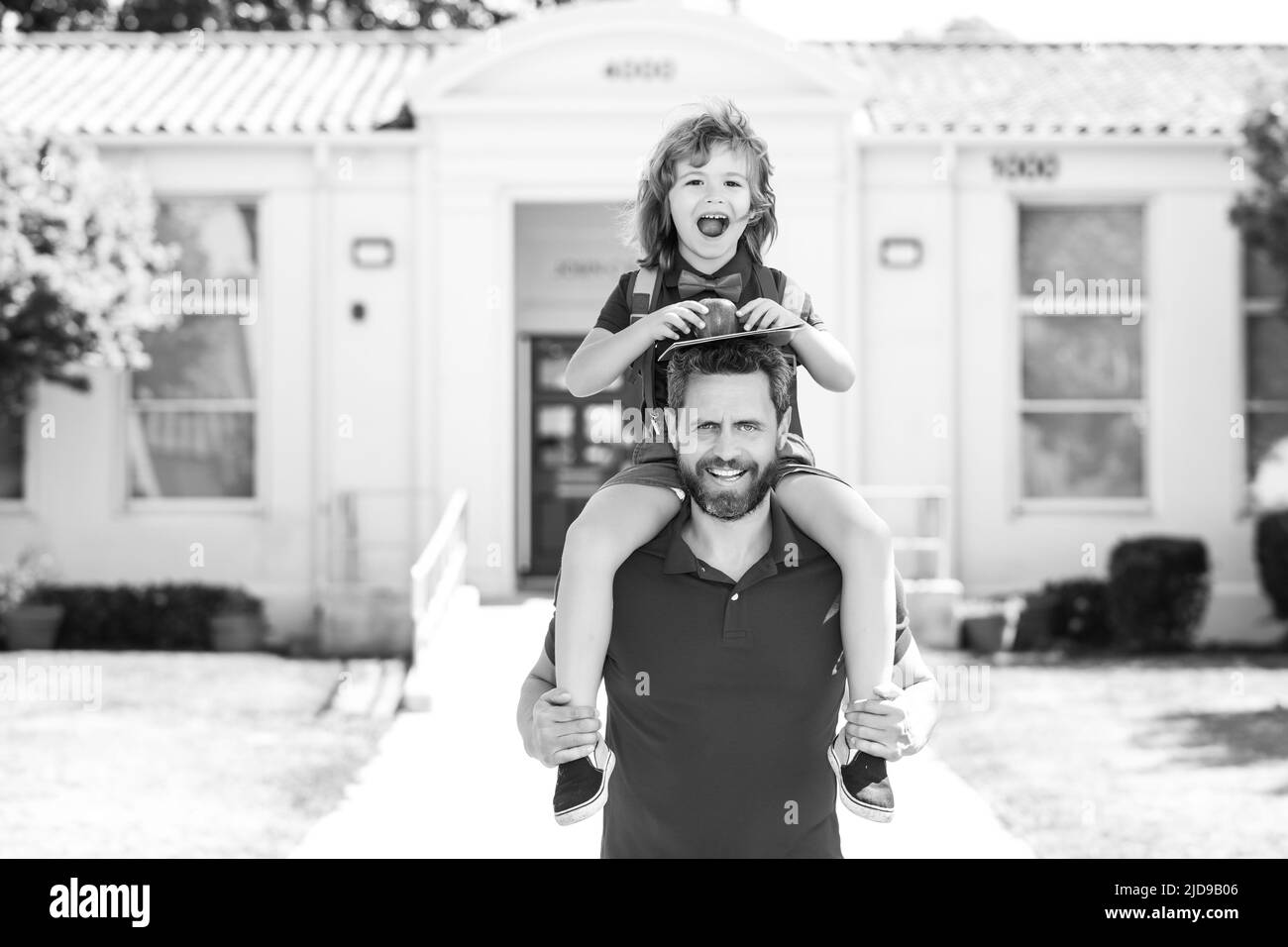 Man and excited amazed child son piggyback near school. Father supports ...