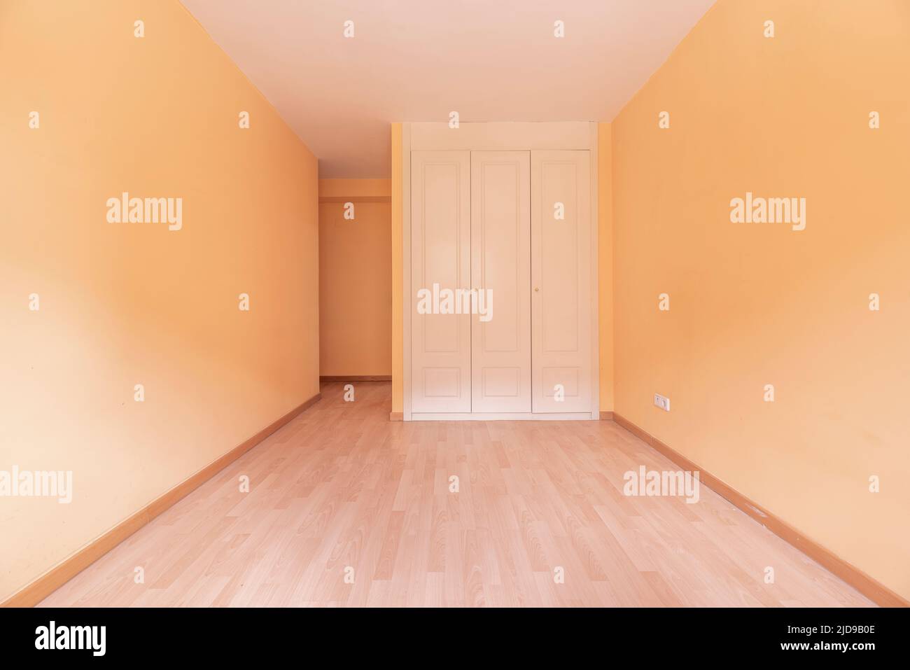 Empty room with white wooden three-body built-in wardrobe and light ...