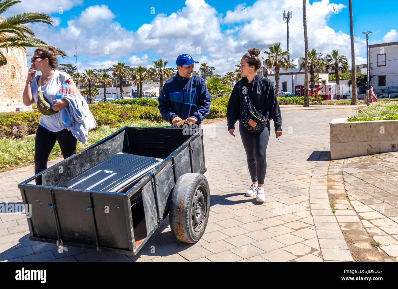 A helper carrying the luggage in a wheeled hand-operated cart for two ...