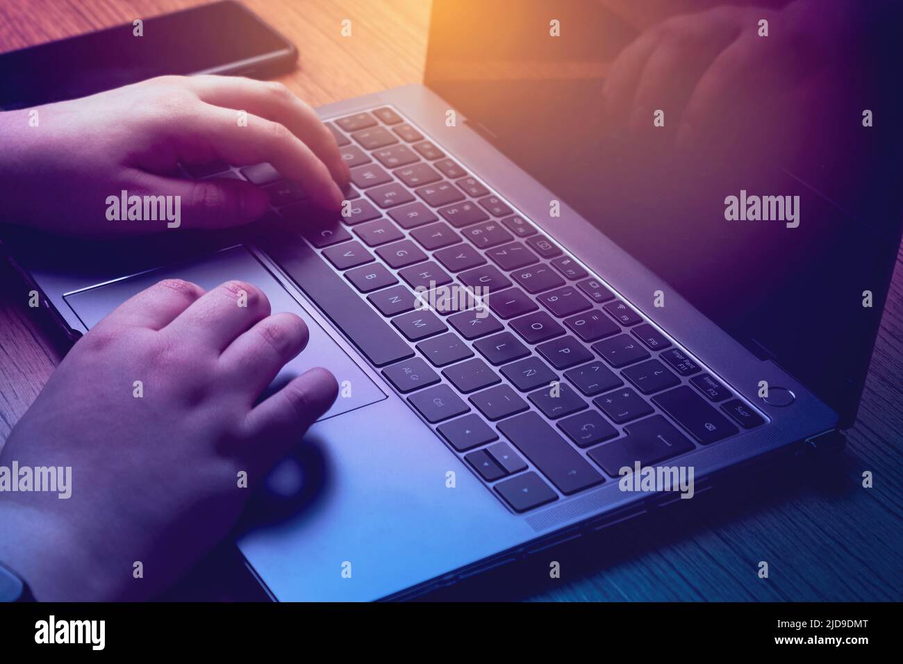 Closeup image of hands typing on laptop with teal light ambient ...