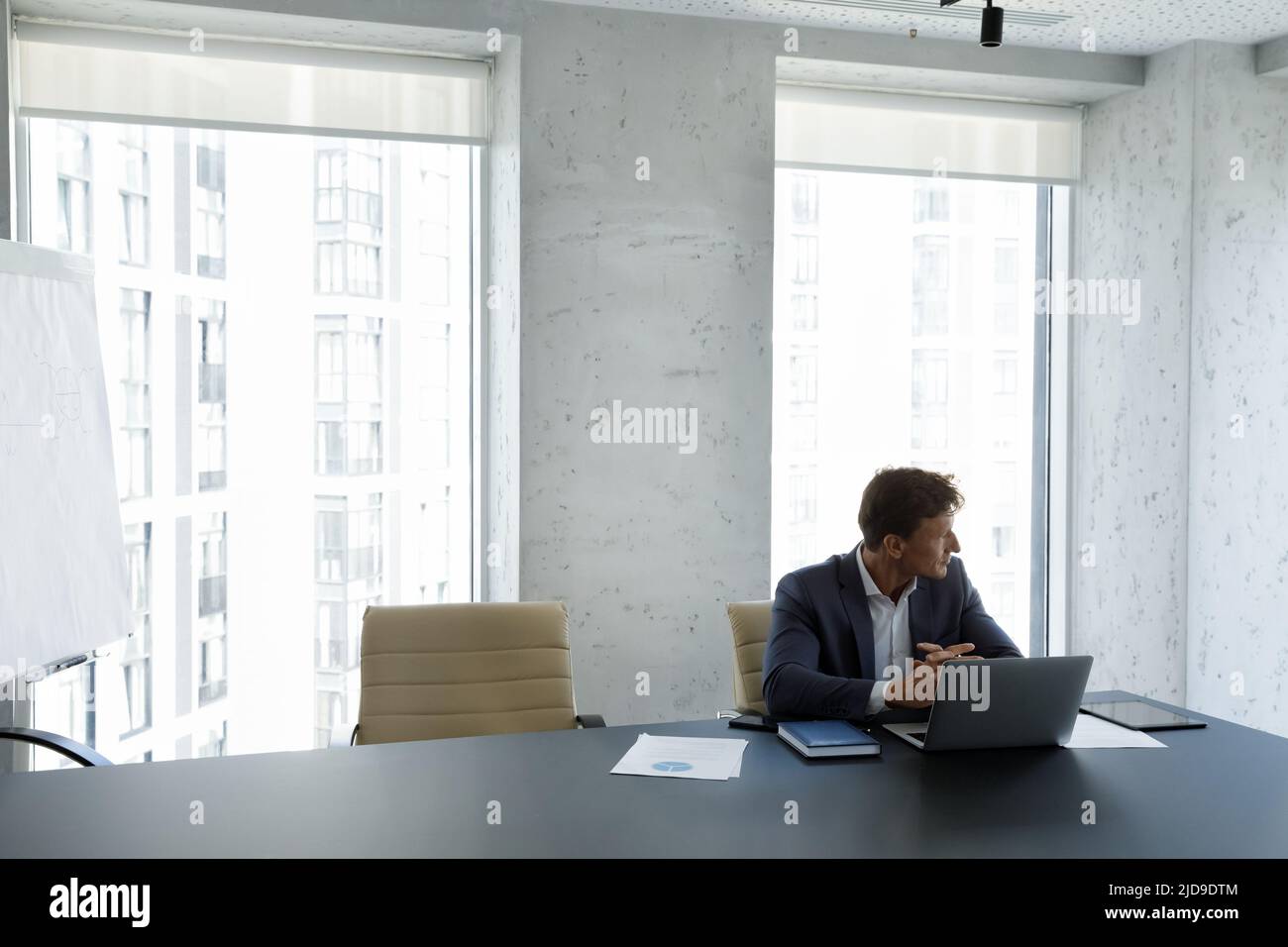Successful businessman staring out window seated at modern skyscraper ...