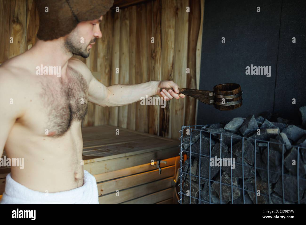 Man pouring water on stones from ladle in sauna Stock Photo - Alamy