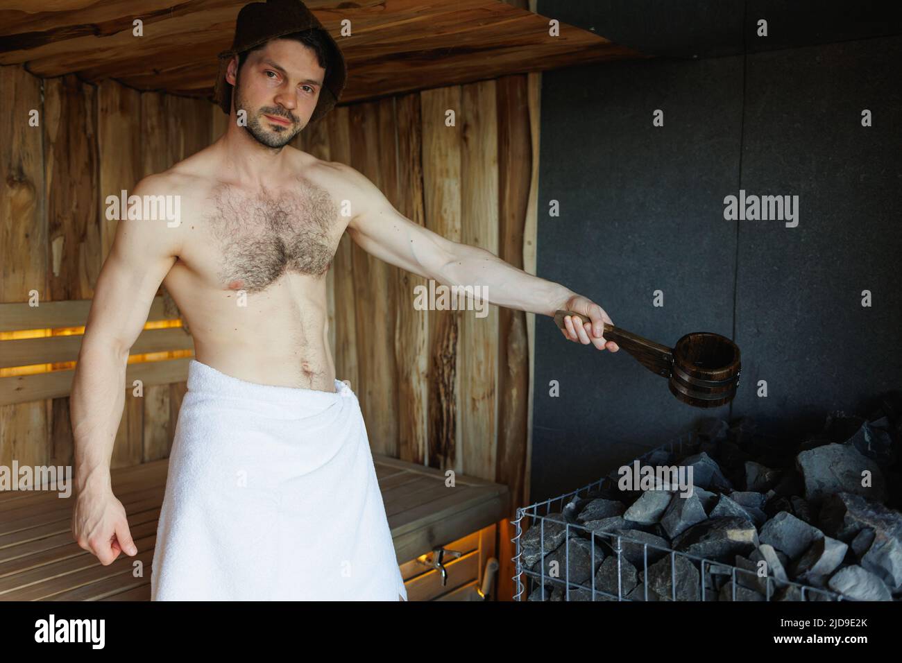 Handsome man pouring water onto hot stone in the sauna Stock Photo - Alamy