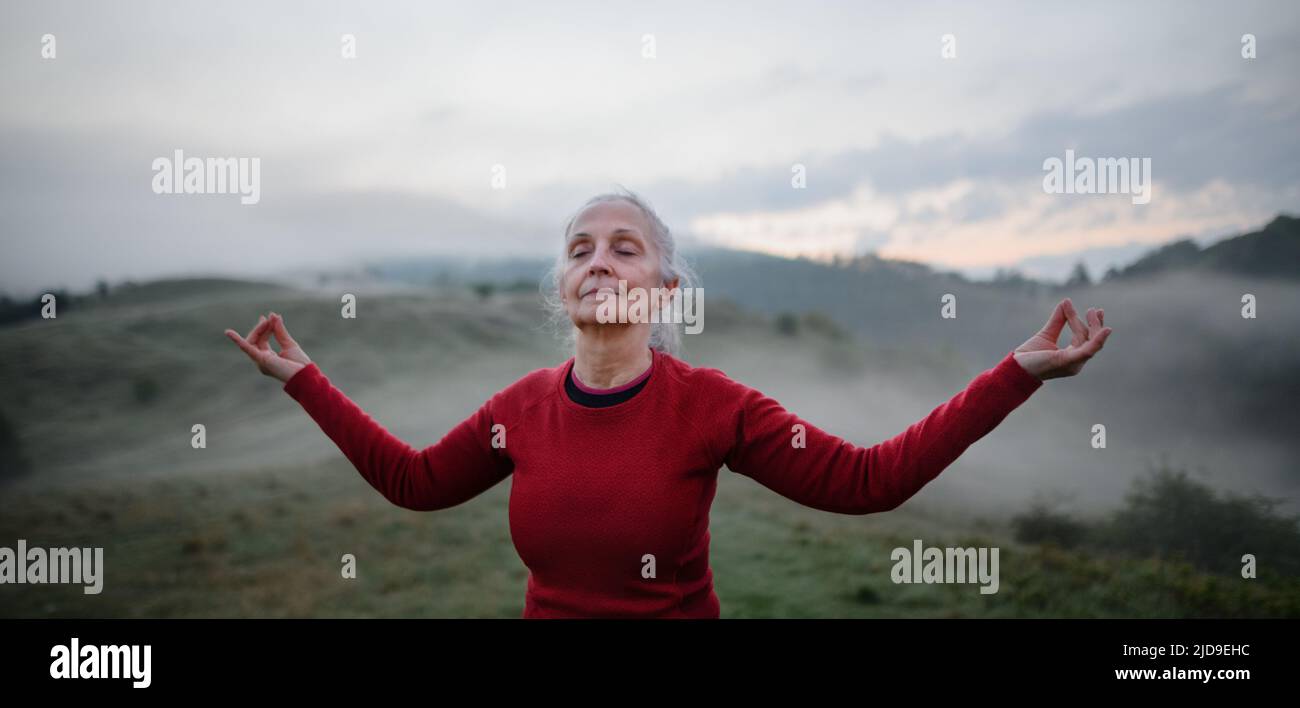 Senior woman doing breathing exercise in nature on early morning with ...