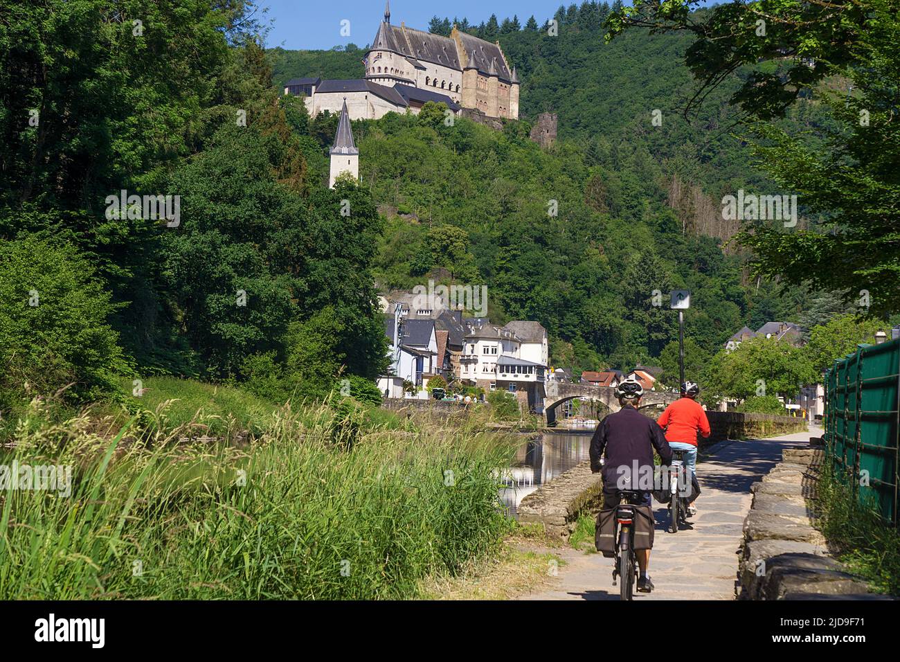 Cyclists on a bike path along the river Our, above the Vianden castle ...