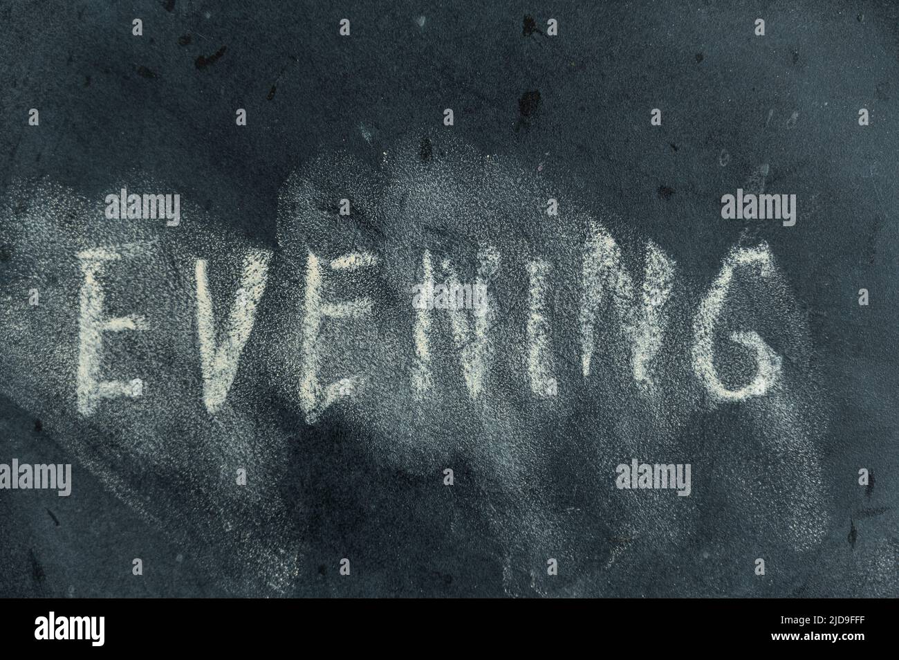 Semi-erased word EVENING on black chalkboard. Handwritten word. Fuzzy ...