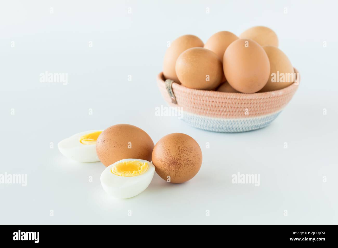 A basket of fresh whole eggs with whole and sliced cooked eggs in front ...