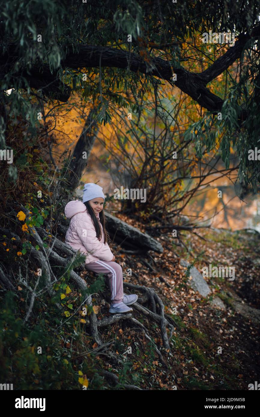 Young Caucasian girl sitting on tree roots in forest, smiling, looking ...