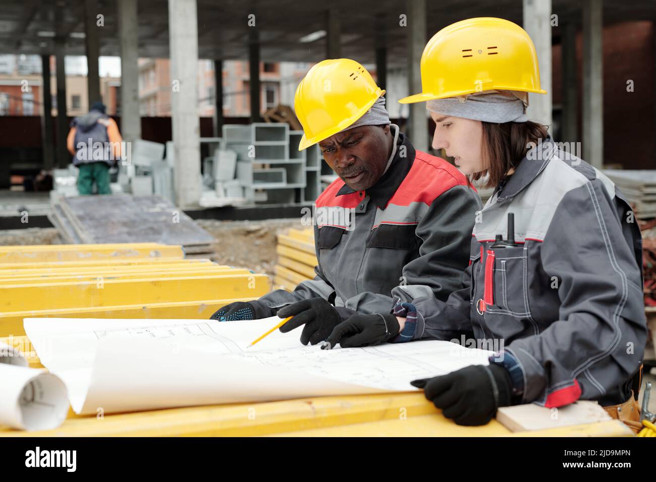 Two confident builders in hardhats and workwear discussing sketch on ...