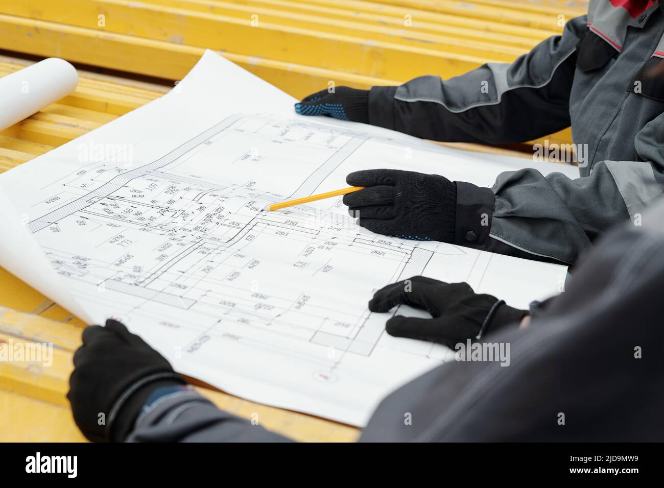 Engineer in gloves and workwear holding pencil while pointing at sketch of building or ...