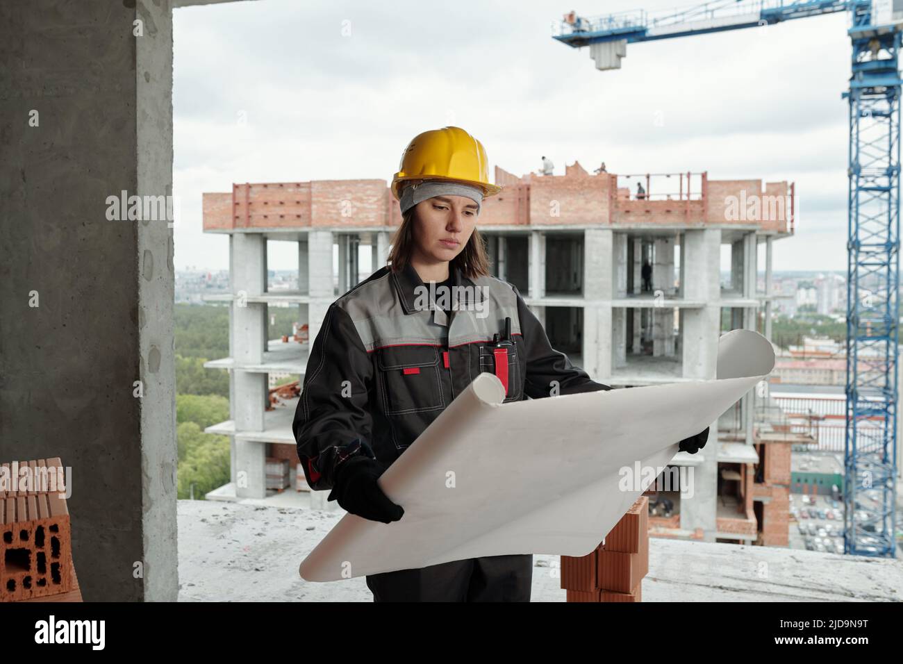 Young female worker of construction site with blueprint standing inside ...