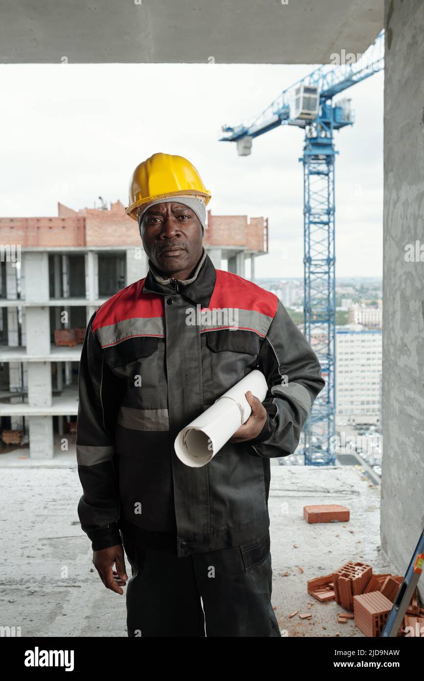 Serious mature foreman with rolled blueprint with architectural plan ...