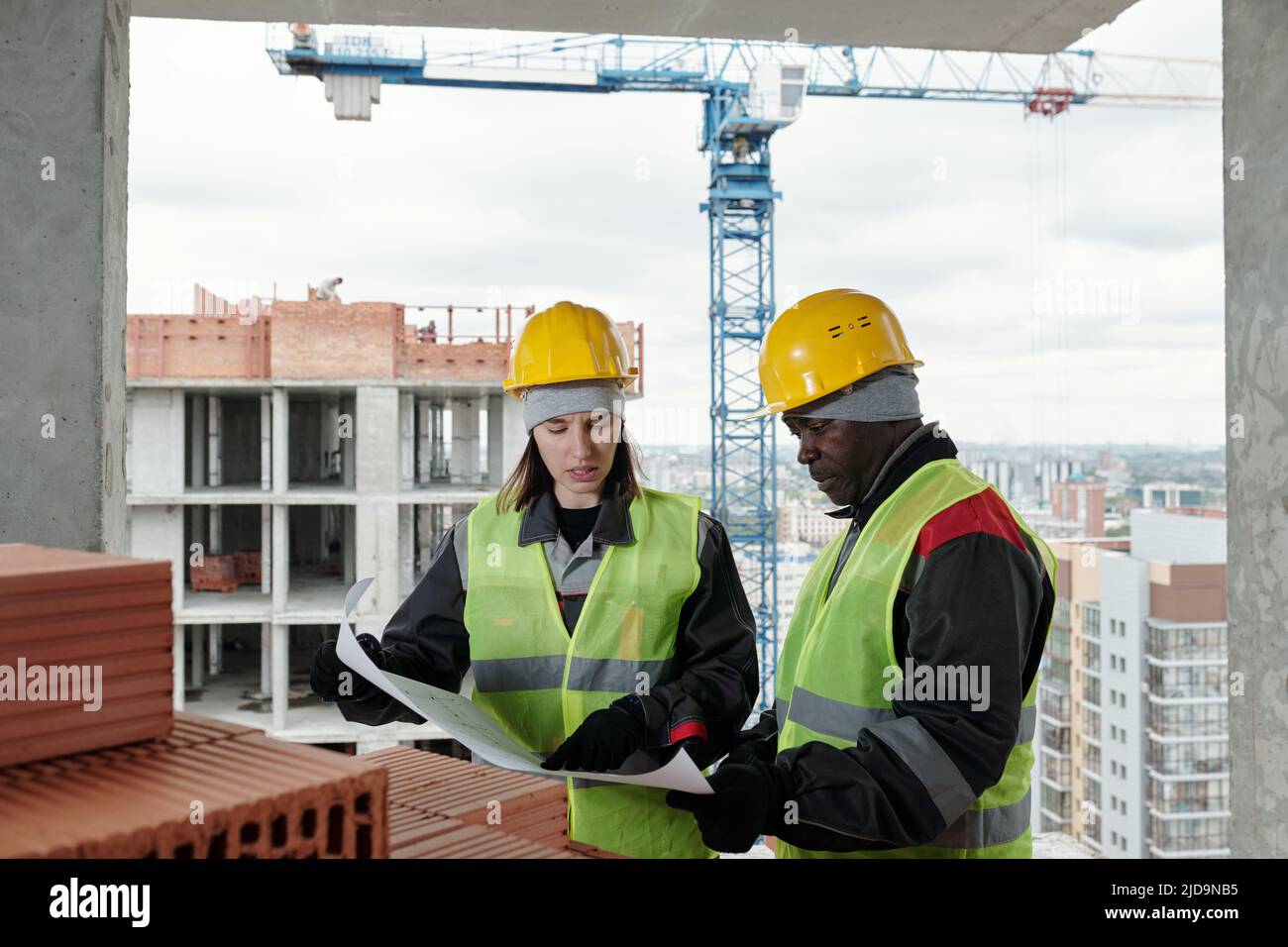 Young female builder and experienced foreman in hardhats and workwear ...