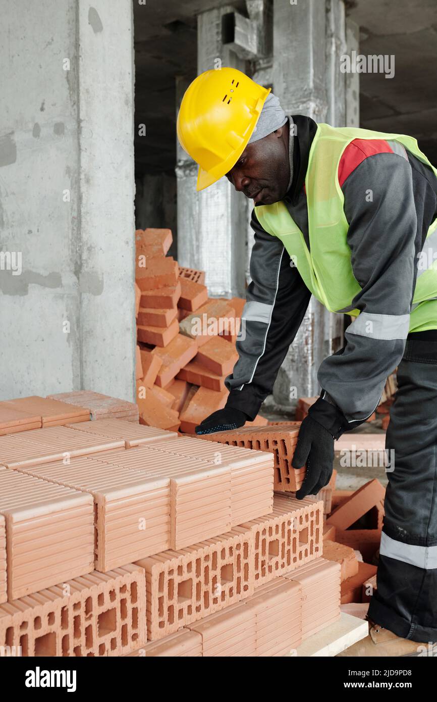 Mature experienced black man in workwear and hardhat bending over stack ...