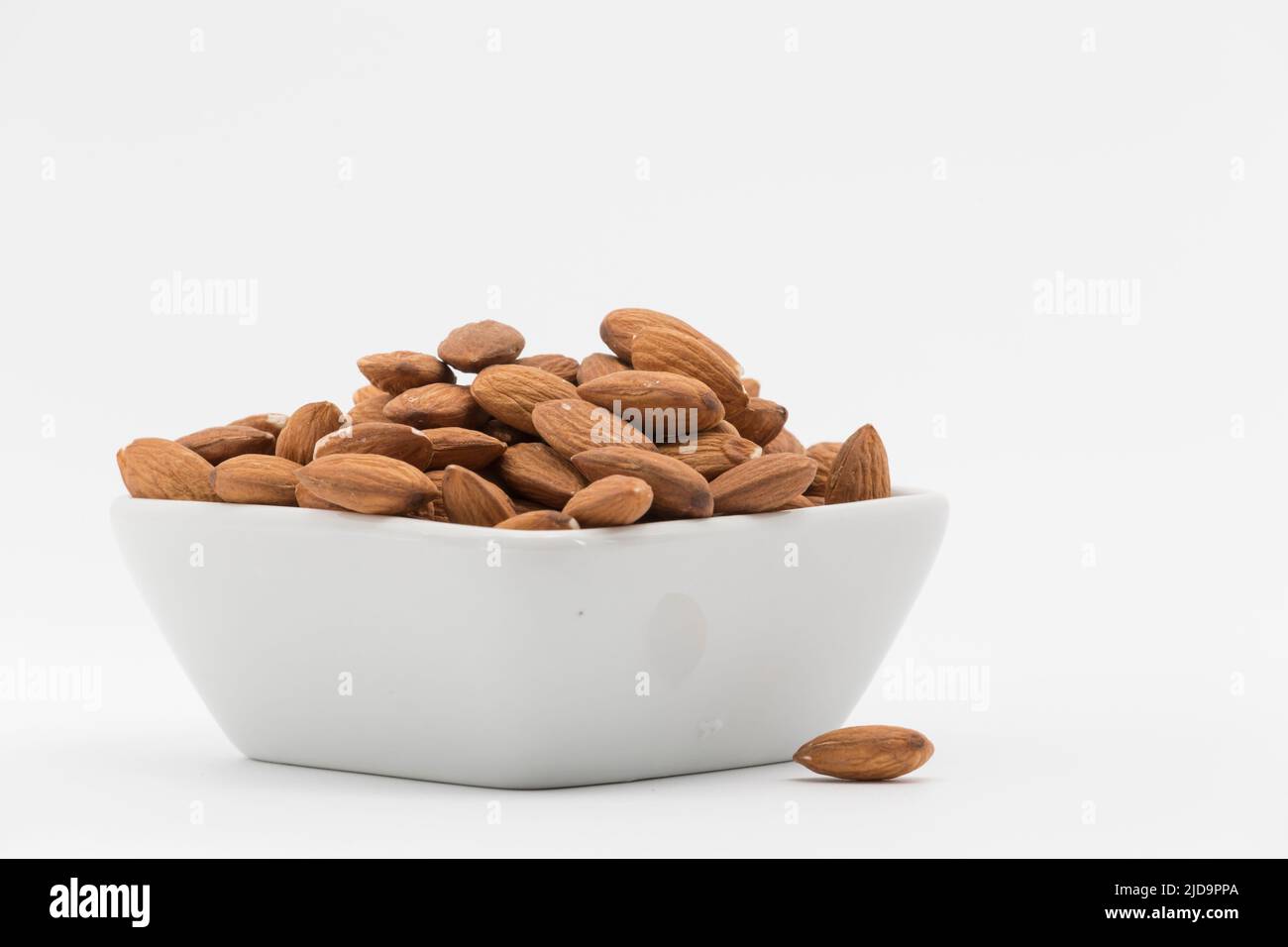view of a square bowl containing a bunch of peeled almonds, placed on a ...