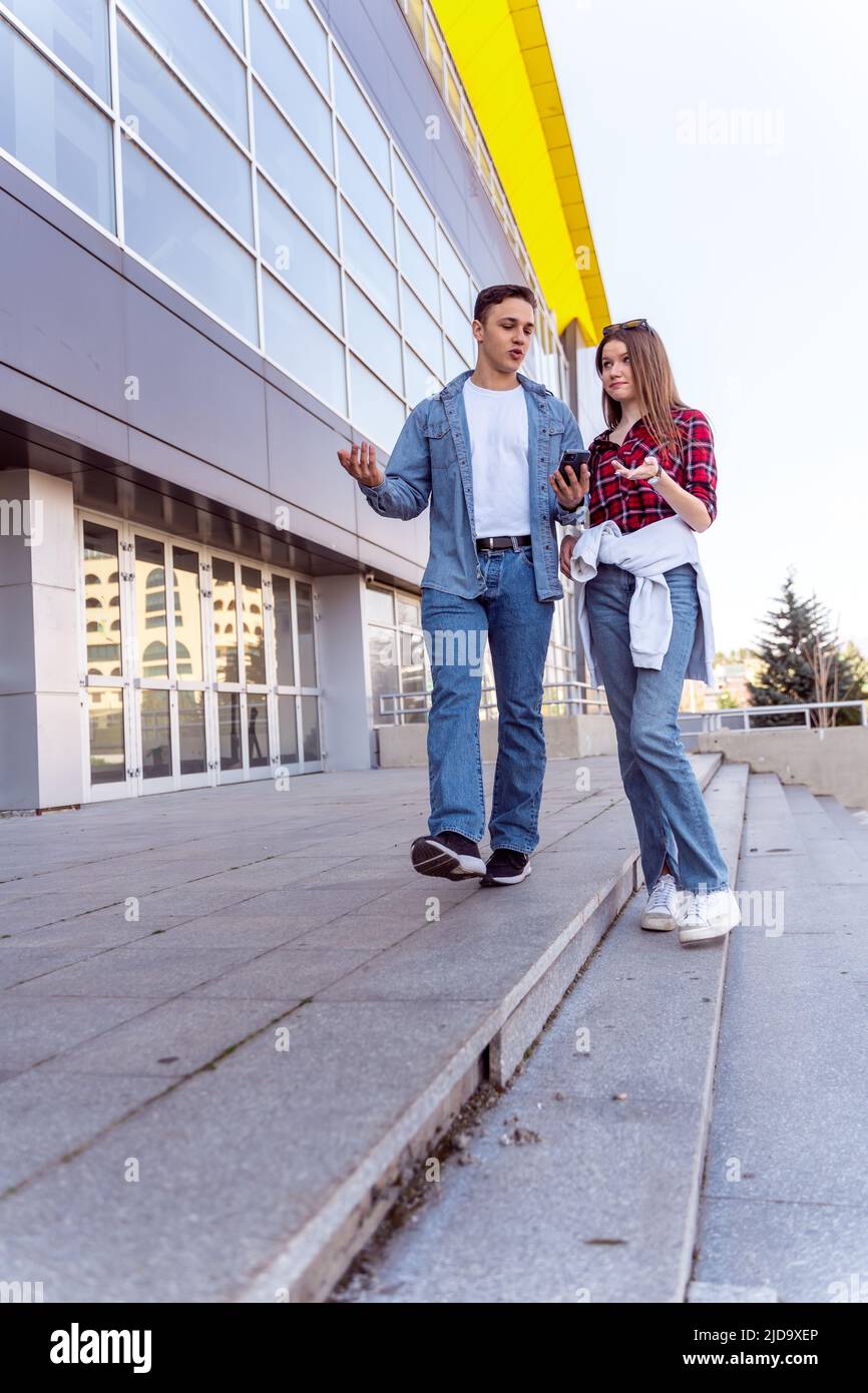 Cute couple talking about something on the phone while walking near the ...