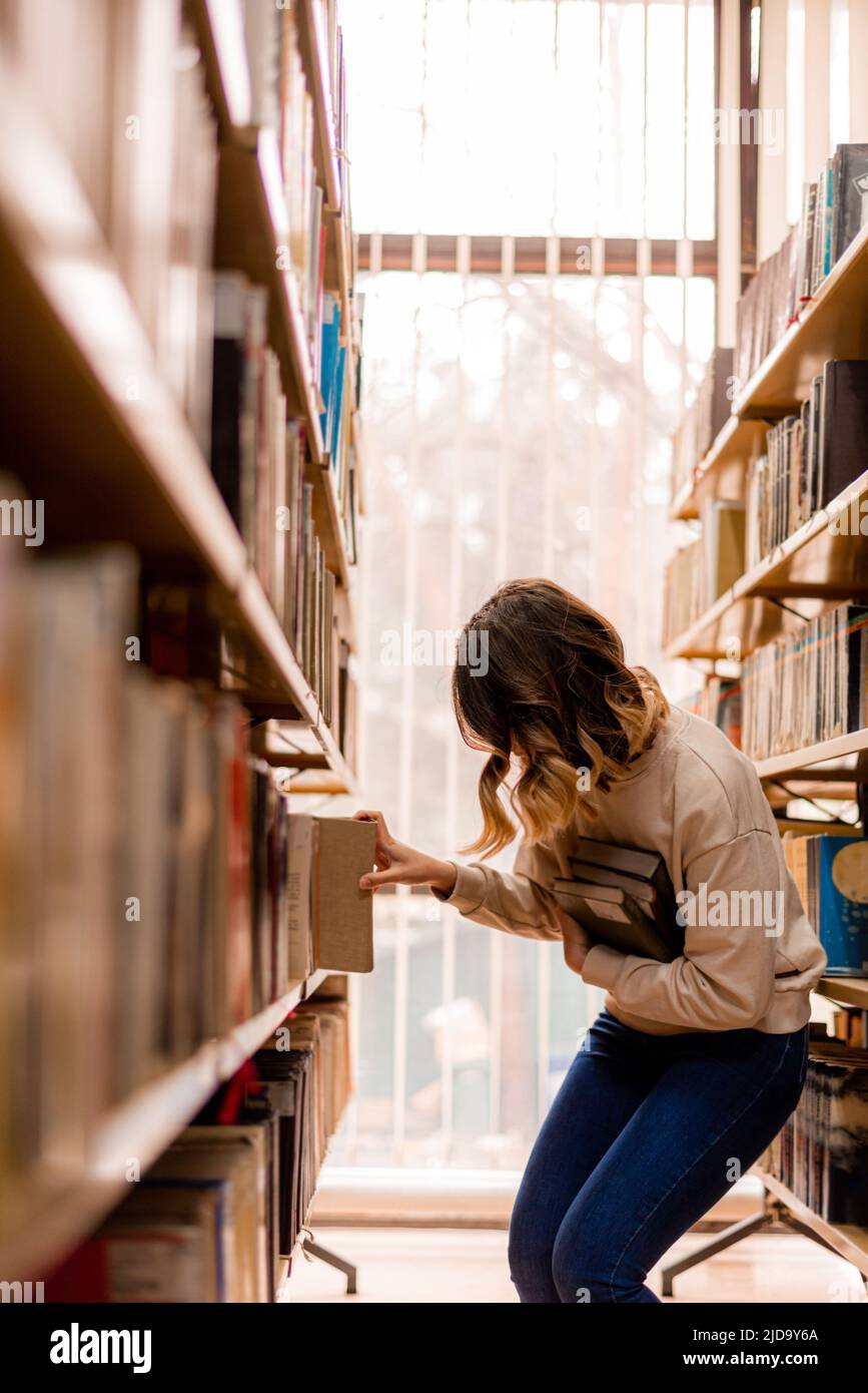Girl taking a book from the bookshelves in the library Stock Photo - Alamy