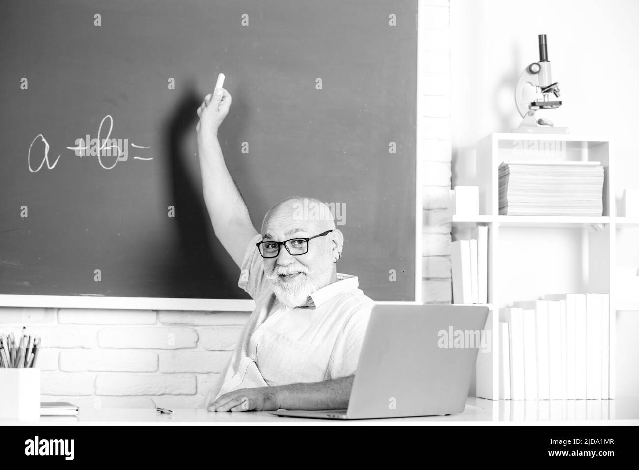 Senior teacher in the classroom on blackboard background. Old professor ...