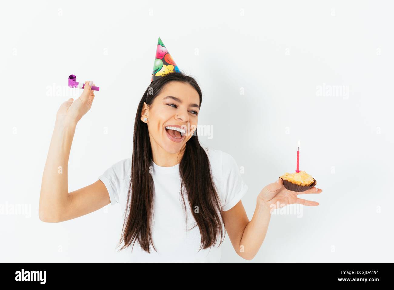 Cheerful carefree young woman in party cap celebrating birthday dancing ...