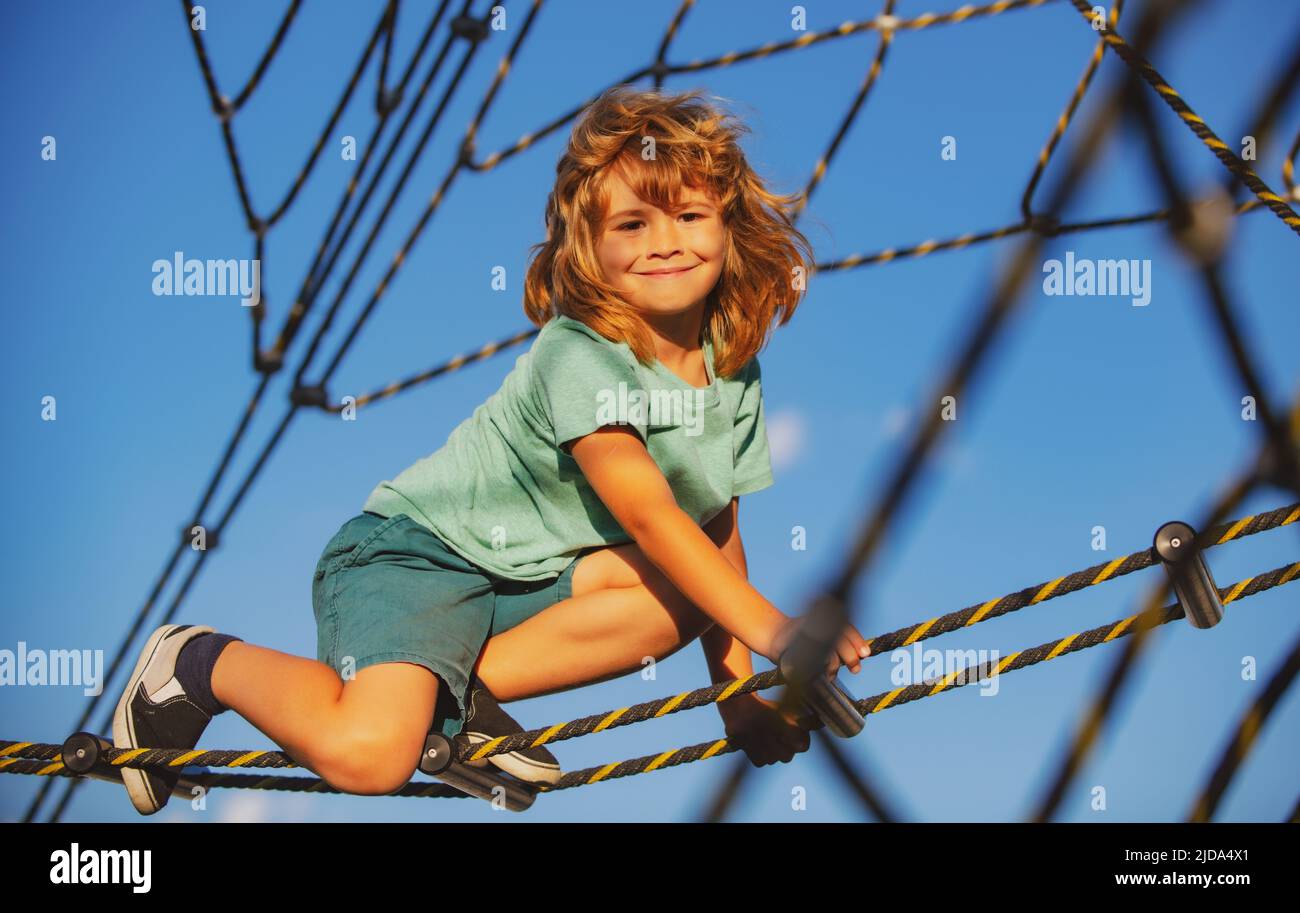 Cute smiling kid climbing the net at the playground. Kids rope park ...