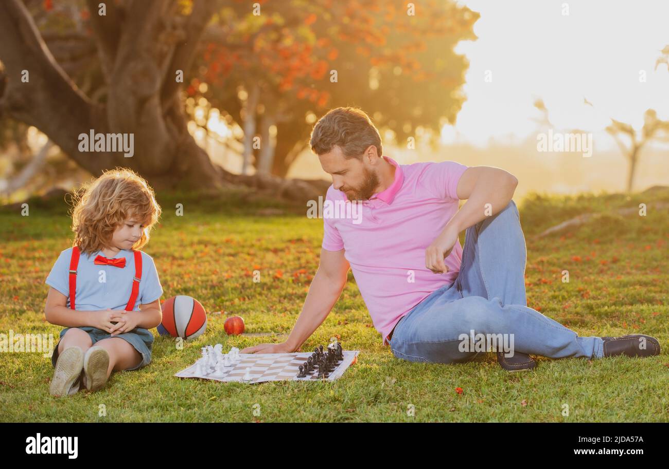 Kid son sitting on grass and playing chess with father. Clever thinking ...