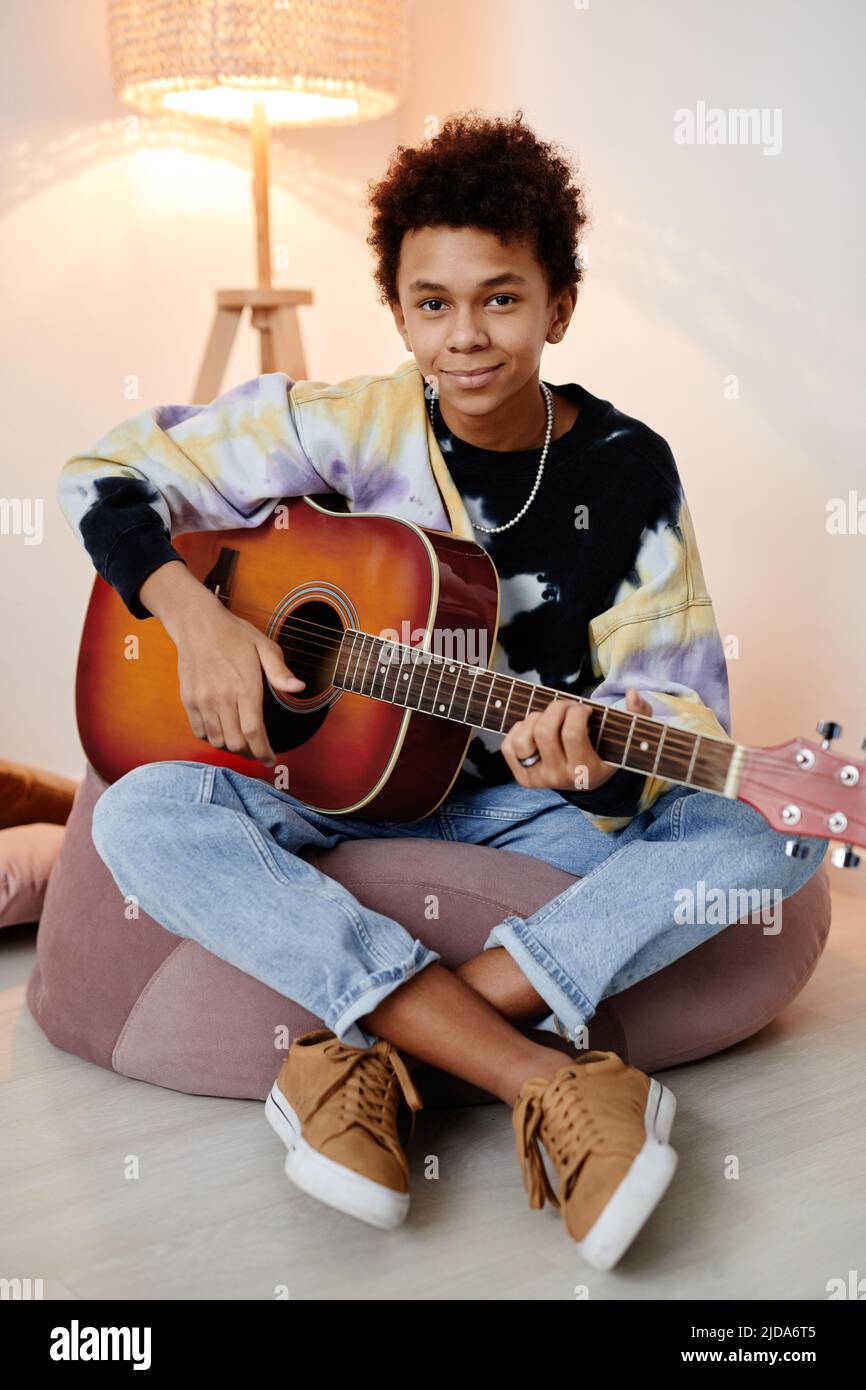 Vertical full length portrait of black teenage boy playing guitar and ...