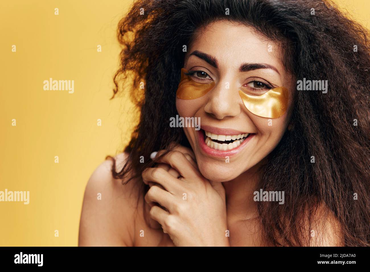 Happy curly pretty Latin female with gold hydrogel patches under eye ...