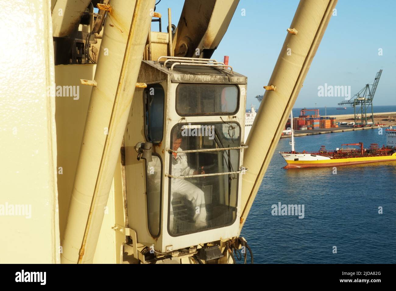 Crane operator in white overall in the cabin of the ship`s crane of ...