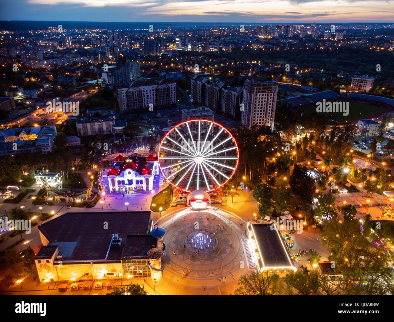 Aerial bright illuminated Ferris wheel with fountain and attractions ...