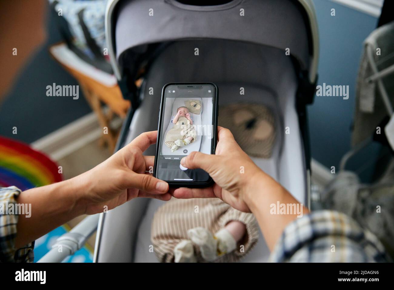 Mother taking photograph of 3 month old baby boy lying in baby buggy ...
