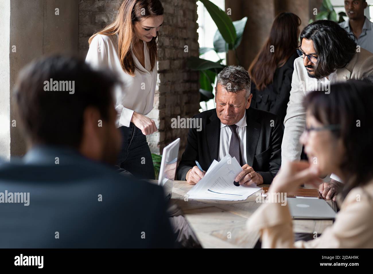 Businesspersons signing a contract together gathered around the ...