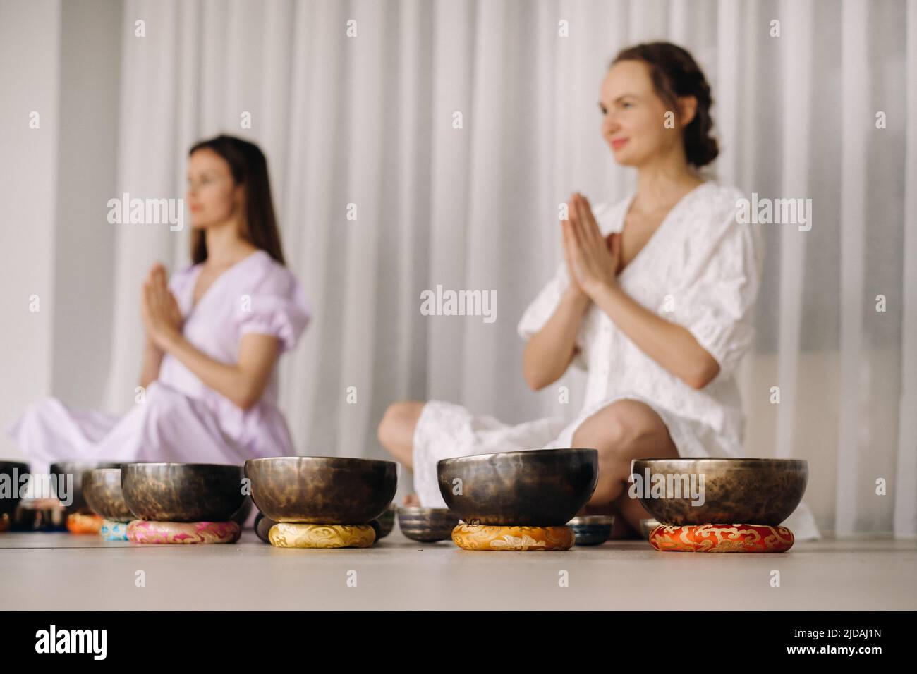 Two women are sitting with Tibetan bowls in the lotus position before a ...