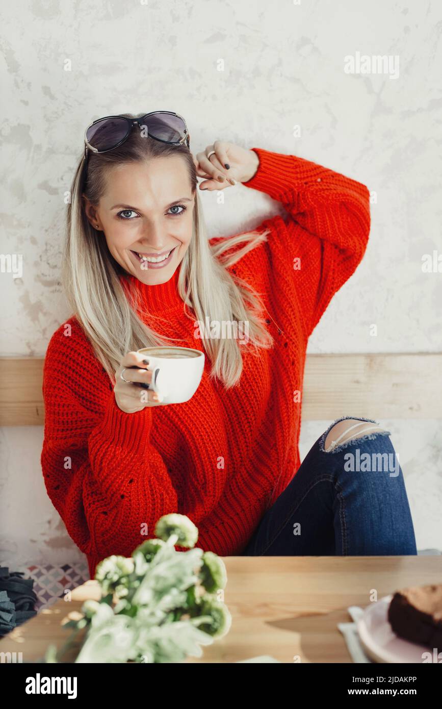 Pretty young women in red sweeter drinking hot coffee in cafe. Person ...