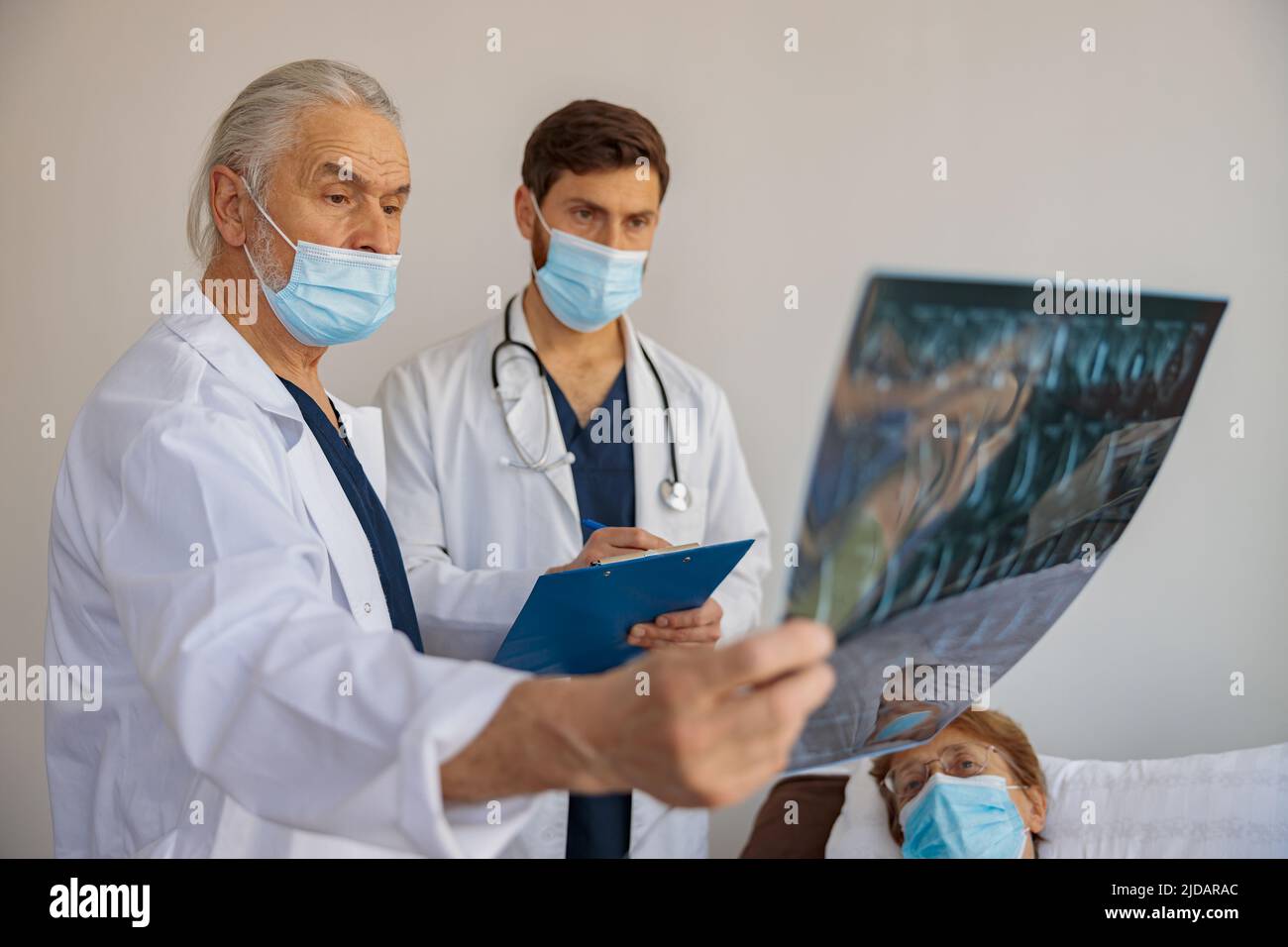 Two doctors in mask look and discuss an X-ray or MRI scan of the ...