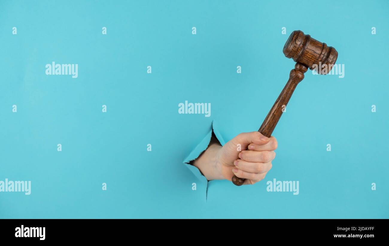 A woman's hand with a wooden judge's gavel sticks out of a hole in a ...