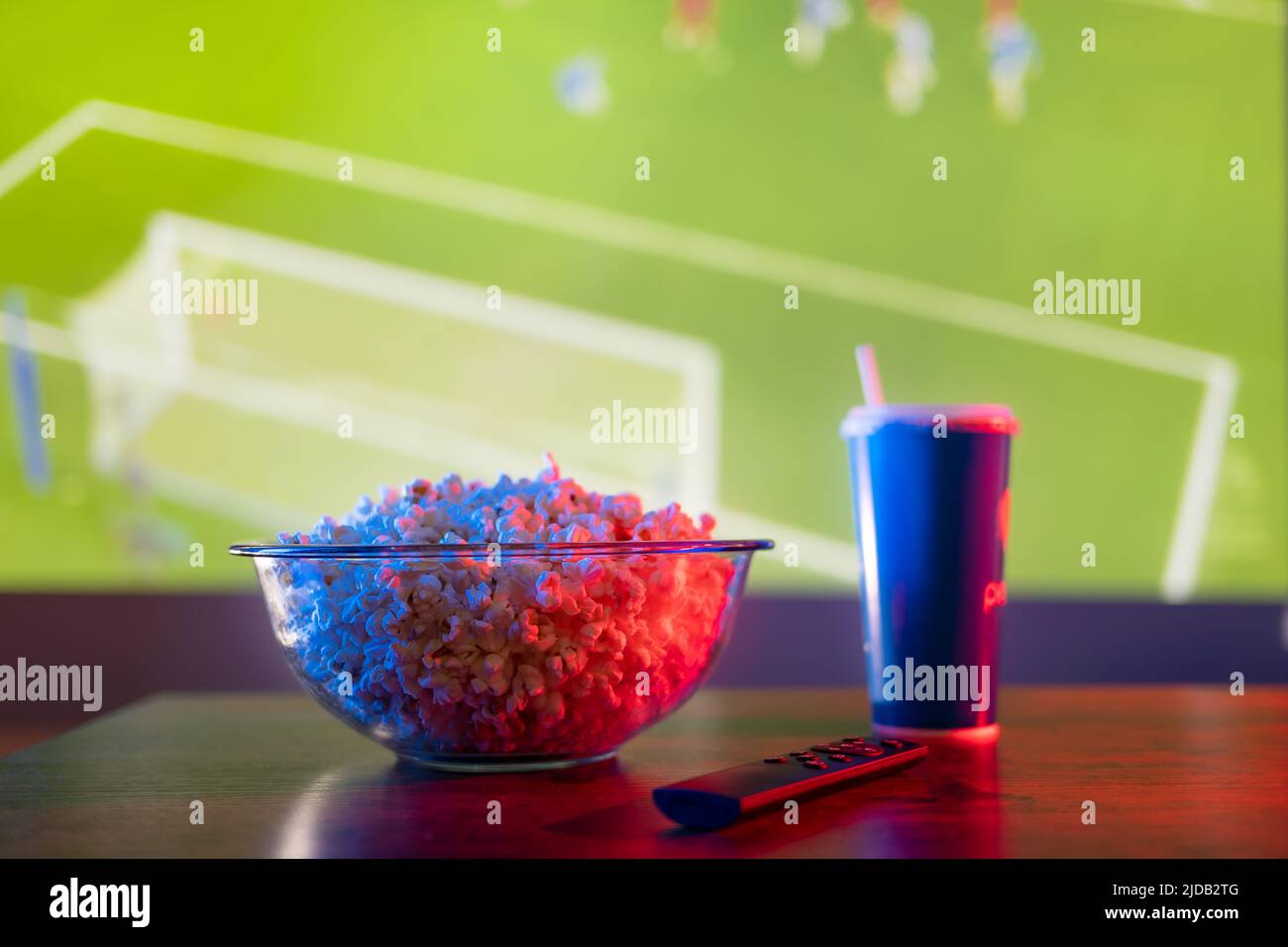 A football match on the big TV screen. Popcorn, a carbonated drink in a ...