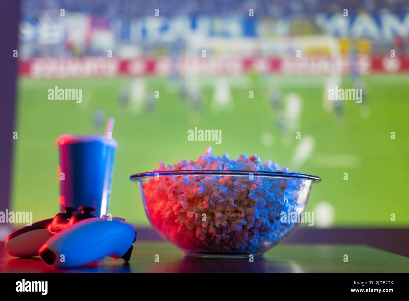 Popcorn in a glass bowl, a drink in a plastic glass and a gamepad on a ...