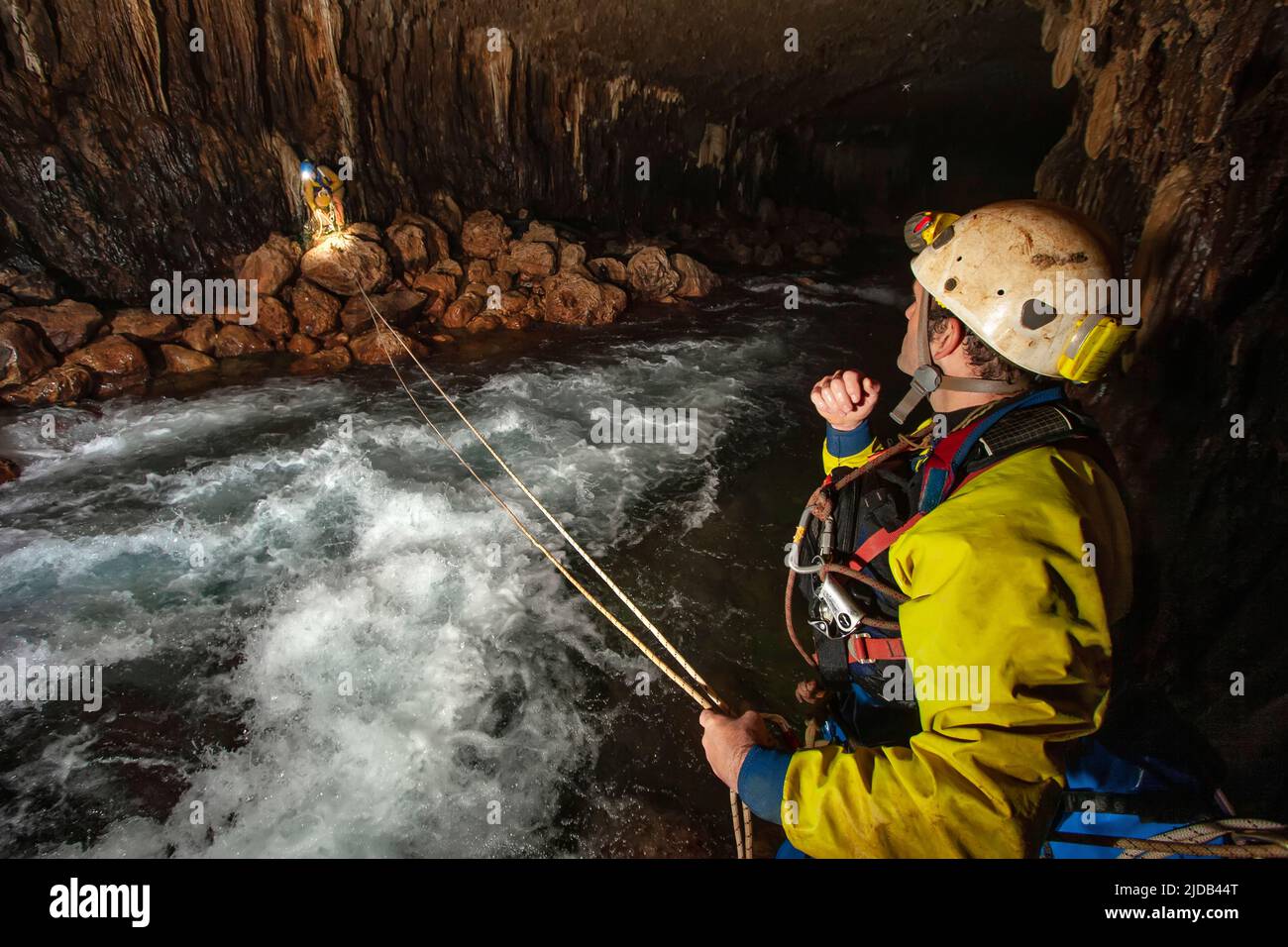 Exploration team members climbing against the rushing river in the Ora cave as they explore the ...