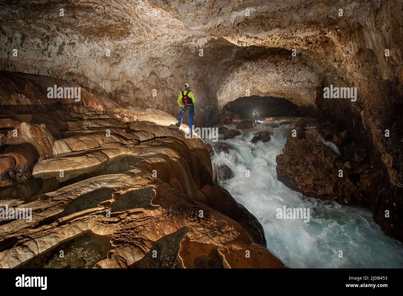 Exploration team members stand along a rushing river in Ora cave as ...