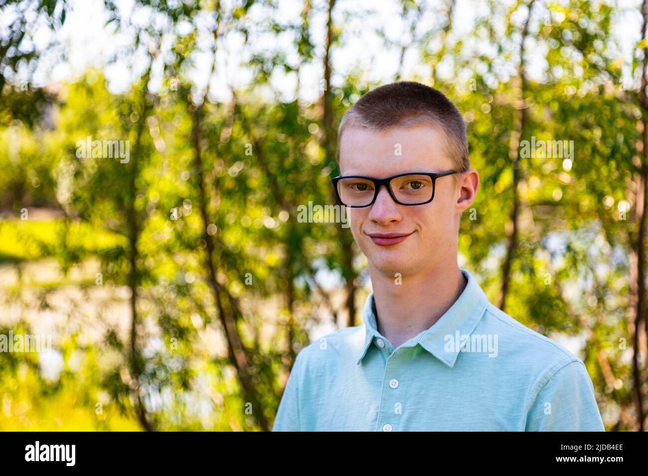 Outdoor portrait of a young man with tree foliage and water in the ...