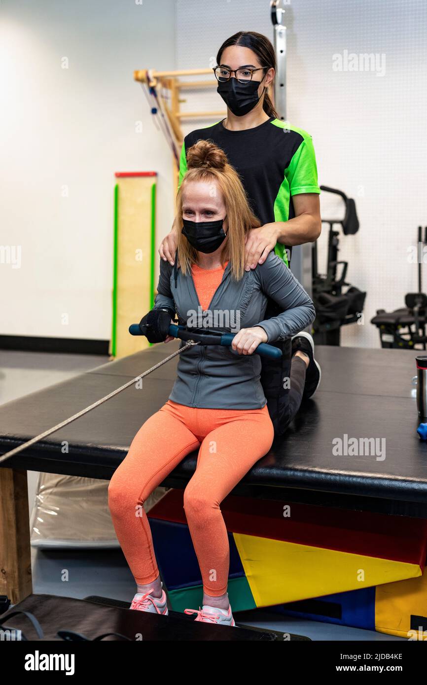 A paraplegic woman working out on a rowing machine with her trainers ...