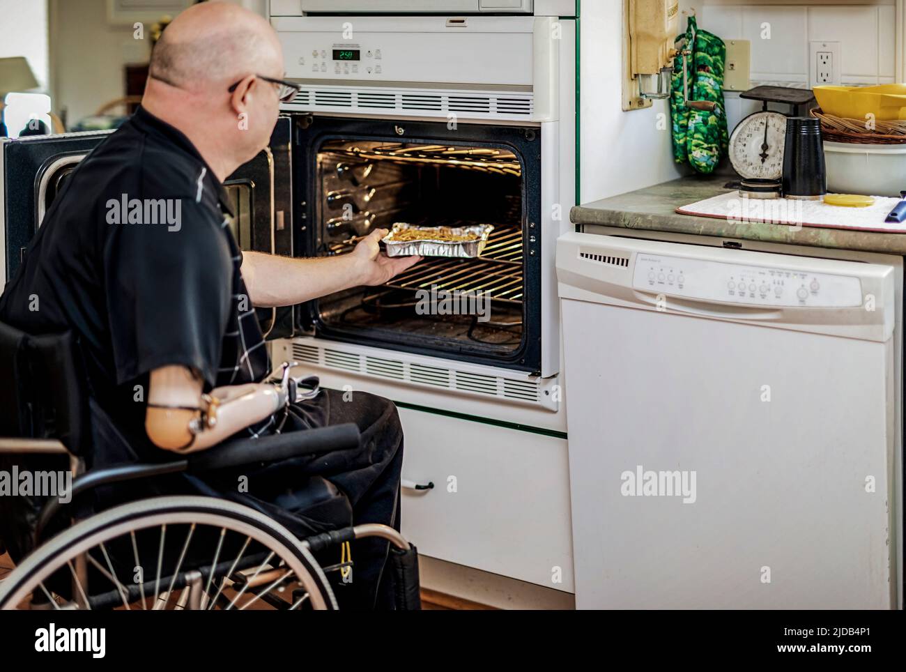 Man with double limb amputations using the oven in the kitchen at home ...