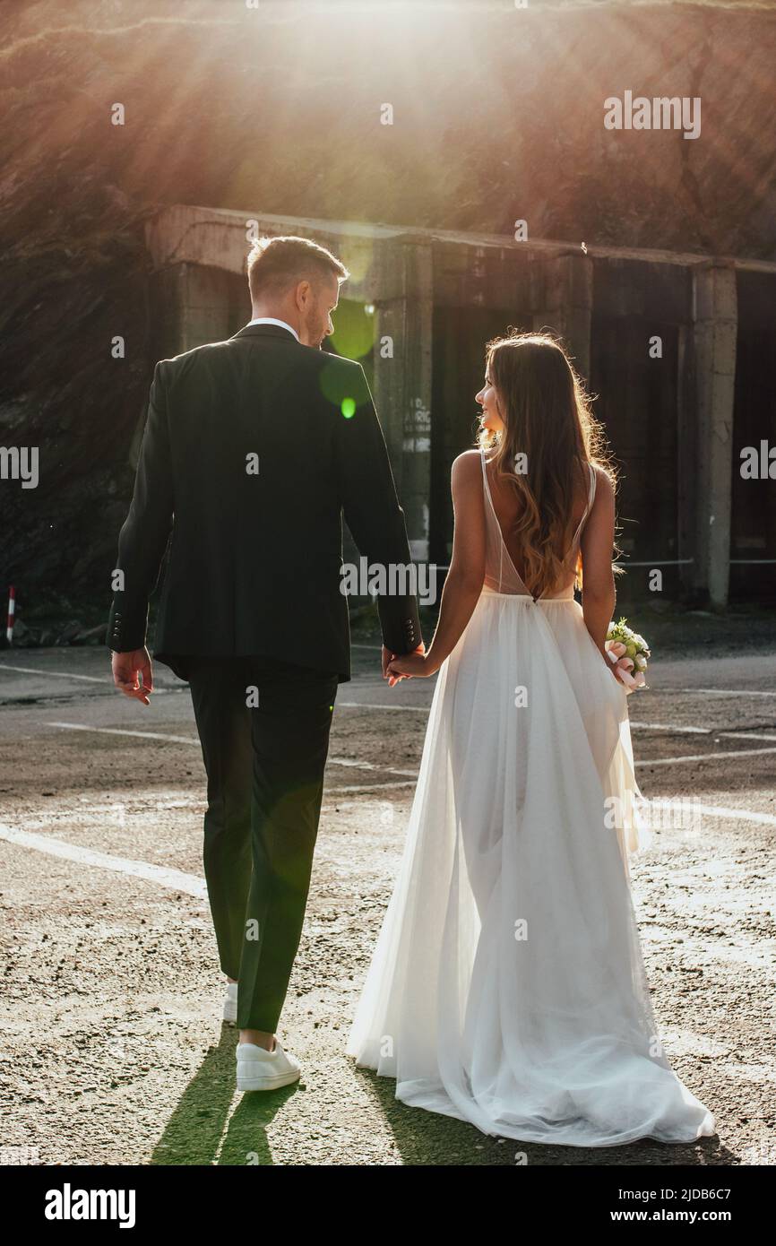 Back view of bride and groom holding hands walking on mountain road ...
