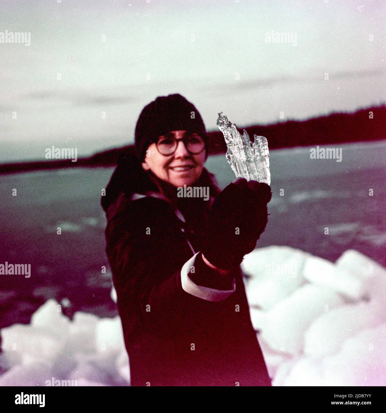 Mature woman stands on the snowy shore of a frozen lake in winter ...